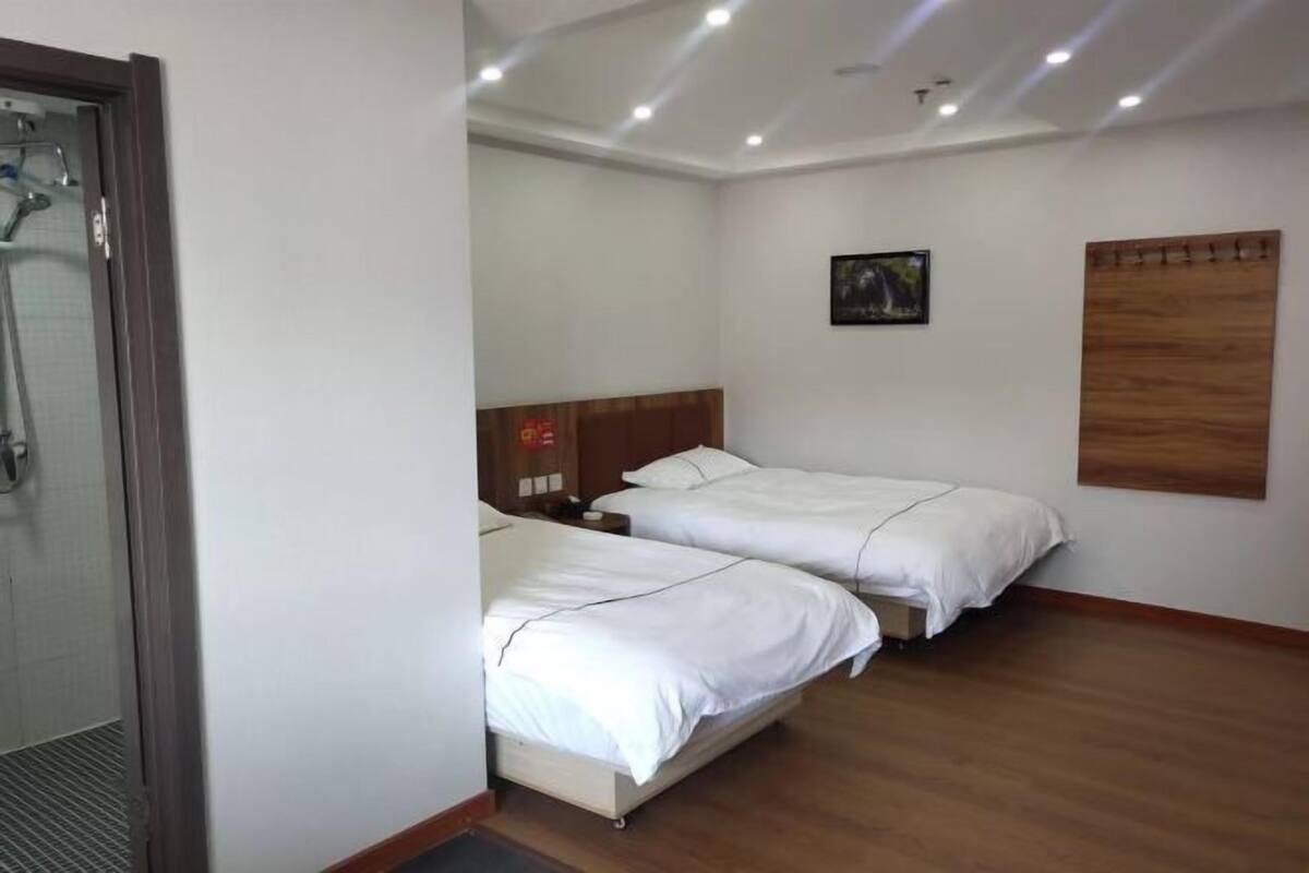 Quarto de hotel com duas camas, chuveiro, cabeceira de madeira, um quadro na parede e um painel de madeira.