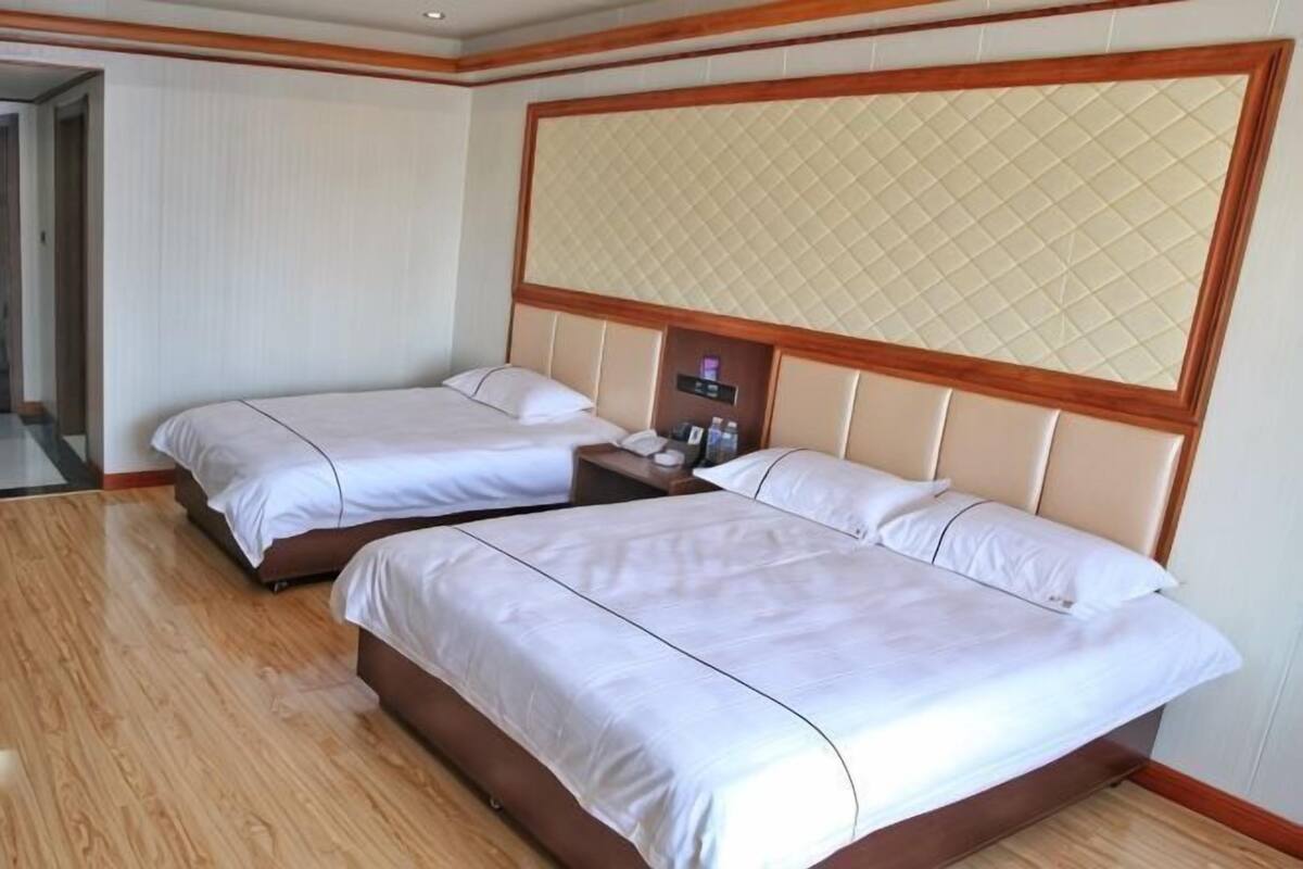 Quarto de hotel com duas camas, uma cabeceira de madeira, uma mesa de cabeceira e uma mesinha de apoio.