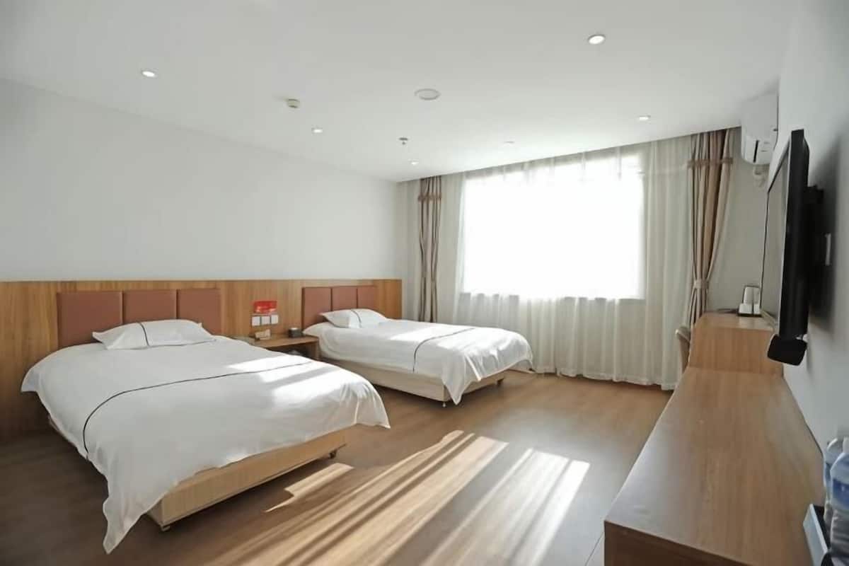 Quarto de hotel com duas camas, cabeceira de madeira, televisão de tela plana e uma janela grande com cortinas.