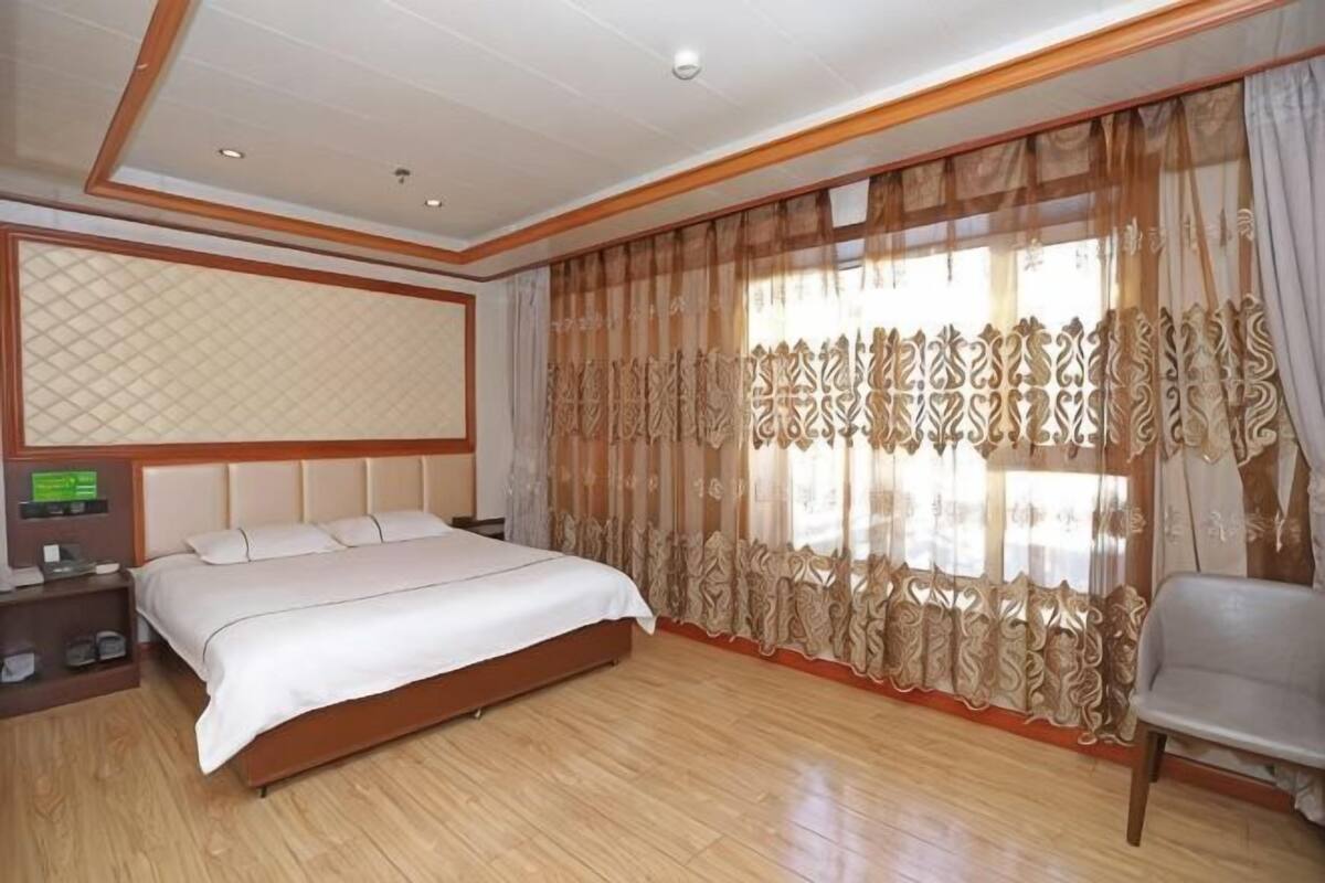 Quarto com cama grande, mesa de cabeceira, cadeira e janela com cortinas.