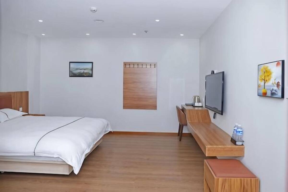 Quarto de hotel com cama, escrivaninha com cadeira, televisão e uma obra de arte na parede.