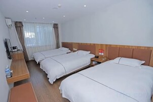 Quarto de hotel com três camas, uma escrivaninha e uma televisão.