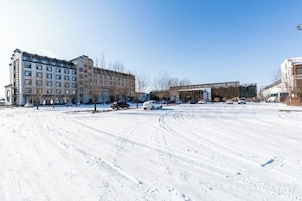 Um estacionamento coberto de neve, com edifícios ao fundo.