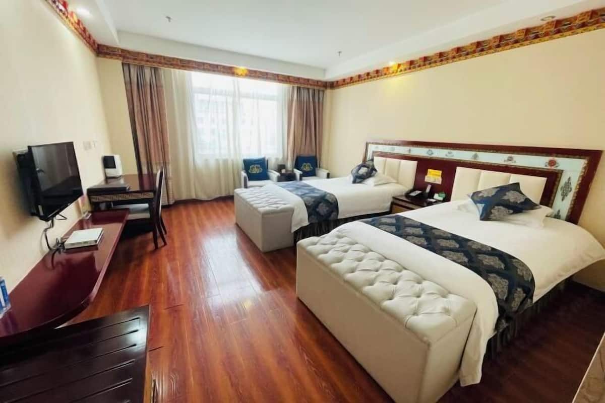 Quarto de hotel com duas camas, uma escrivaninha com televisão e uma janela com cortinas.