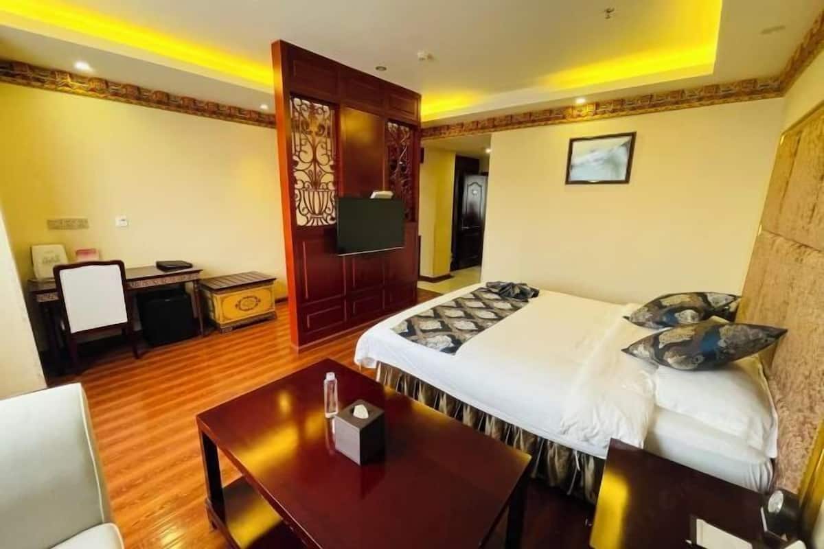 Quarto de hotel com uma cama grande, uma mesa, uma cadeira, uma televisão e um armário de madeira.