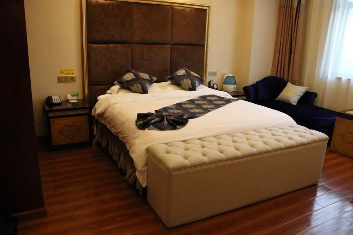 Quarto de hotel com uma cama grande, mesa de cabeceira, uma cadeira e uma janela com cortinas.