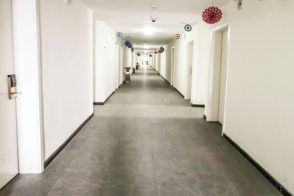 Corredor de hotel comprido e estreito, com portas em ambos os lados e um caminho central.