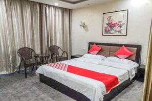 Quarto de hotel com cama, duas cadeiras, mesa pequena, mesa de cabeceira e um quadro na parede.