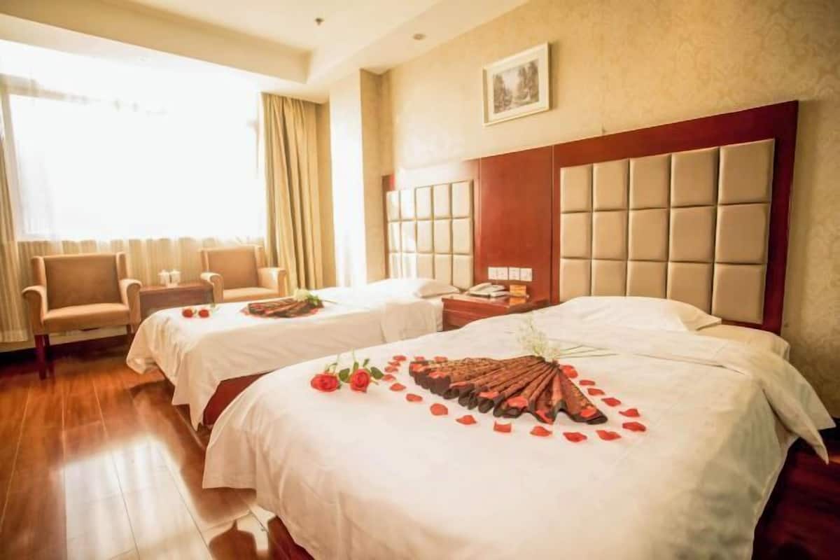 Quarto de hotel com duas camas, um espaço de estar com cadeiras e uma janela grande.