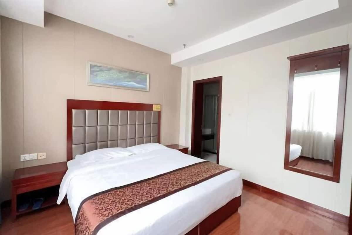 Quarto de hotel com uma cama grande, cabeceira de madeira, mesa de cabeceira, espelho e um quadro na parede.
