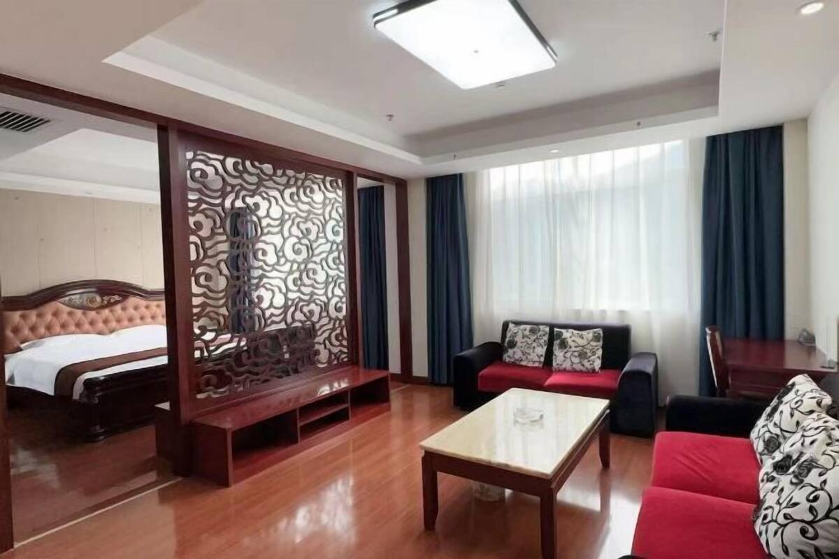 Quarto de hotel com cama, sofá, mesa de centro e divisória decorativa.