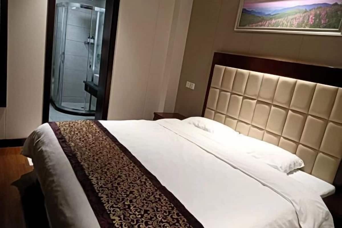 Quarto de hotel com cama, cabeceira, chuveiro e uma pintura na parede.