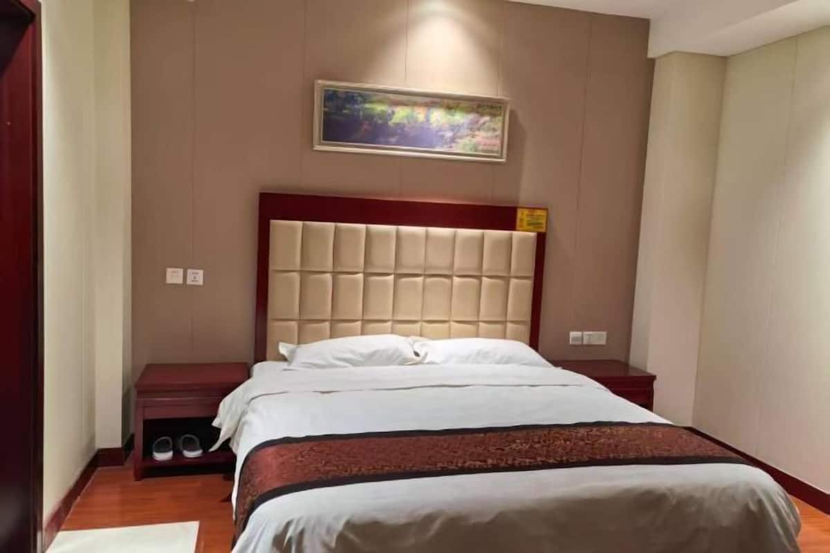 Quarto de hotel com uma cama grande, cabeceira, mesa de cabeceira e um quadro pendurado na parede.