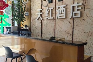 Bancada de recepção de hotel com parede de mármore e uma placa com a inscrição '天红酒店'. Há duas cadeiras em frente ao balcão.