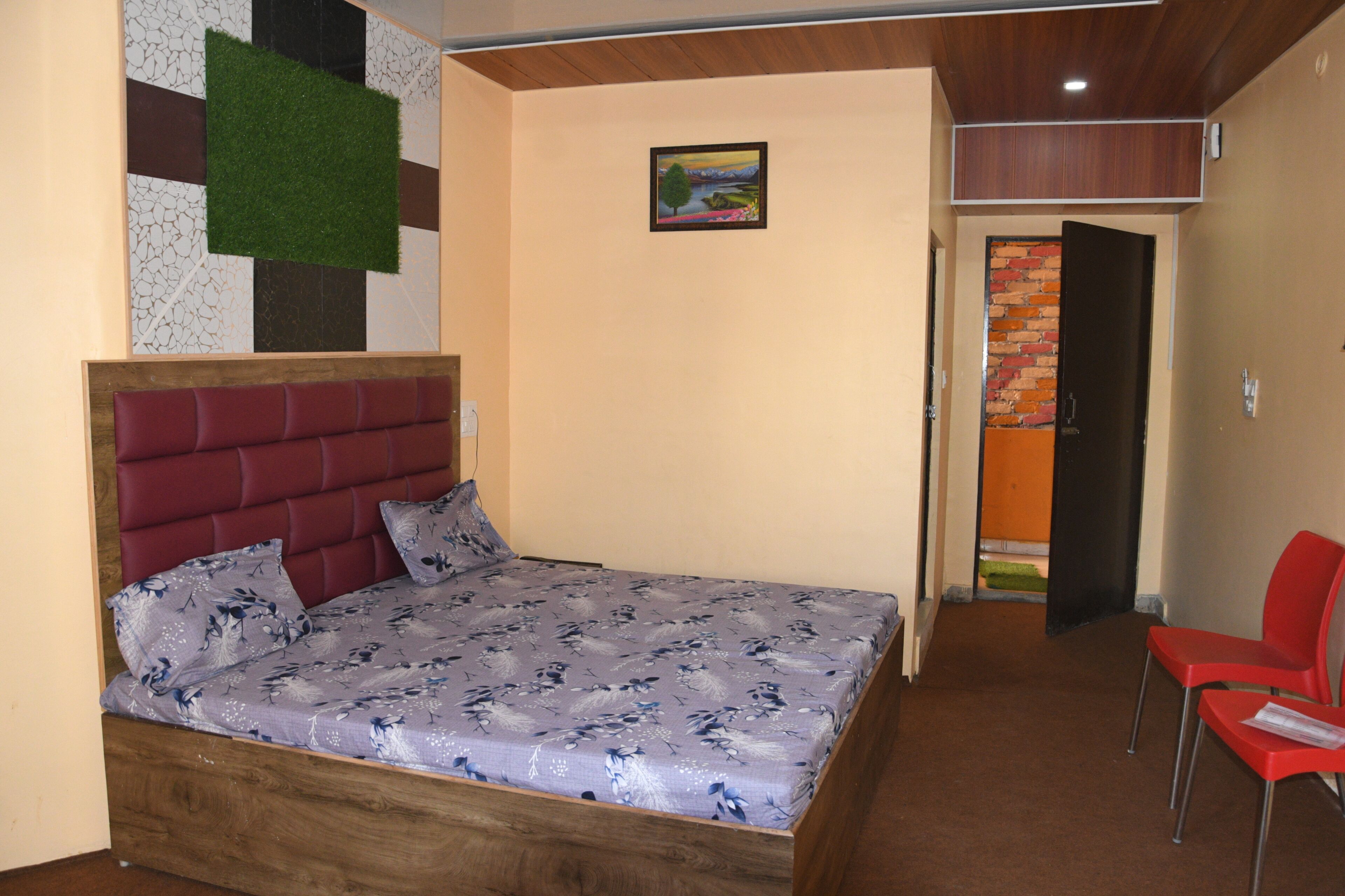 Quarto com cama de madeira, colcha florida, cabeceira estofada em vermelho e uma cadeira vermelha.