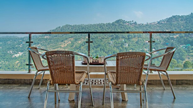 Terraço com cadeiras de vime e uma mesa, com vista para uma paisagem montanhosa.