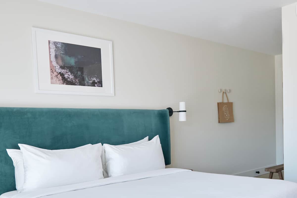 Uma cama grande com cabeceira verde-água, roupa de cama branca e um quadro na parede.