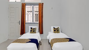 Quarto com duas camas de solteiro, janela com grades de metal, porta e interruptor de luz na parede.