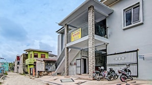 Um edifício de vários andares com varanda, escadaria e entrada protegida por grades.
