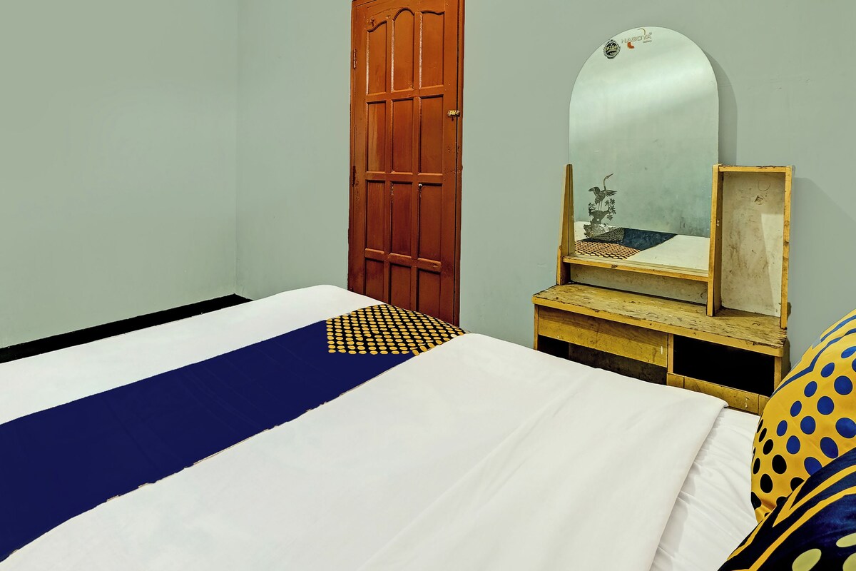 Quarto com cama, porta de madeira, espelho e pequena mesa de madeira.
