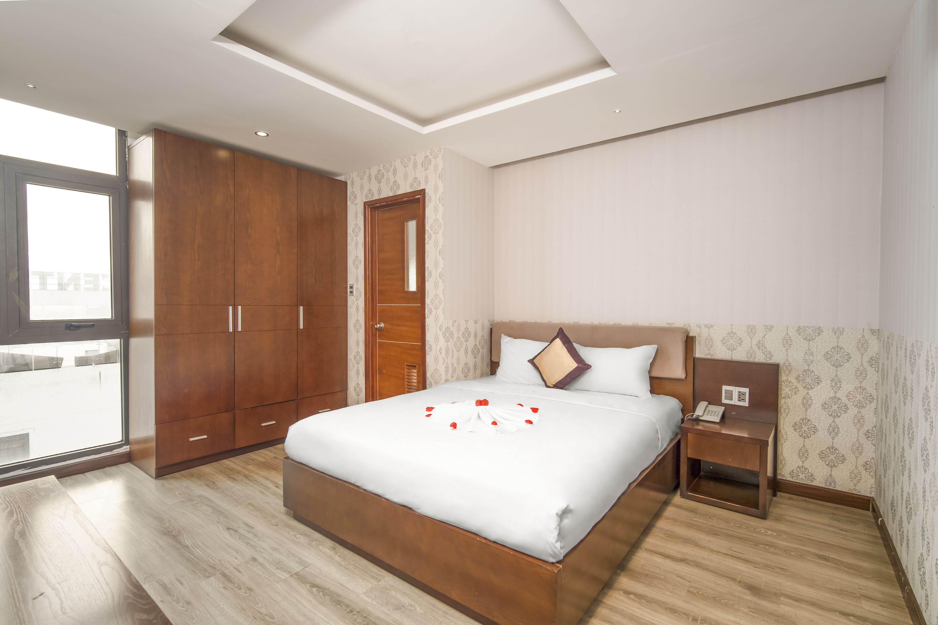 Quarto de hotel moderno com uma cama grande, guarda-roupa de madeira e uma pequena mesa de cabeceira com um telefone.