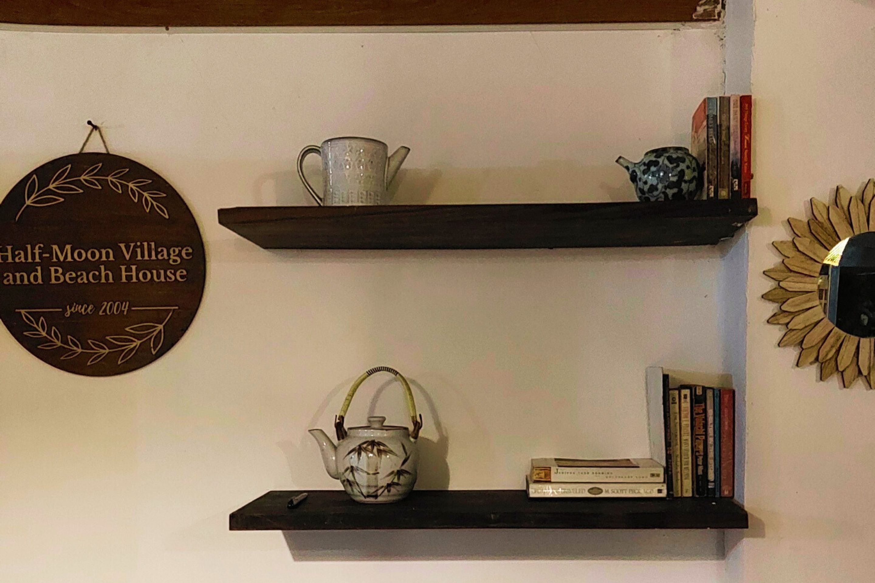Duas prateleiras pretas fixadas na parede, com objetos decorativos, uma placa na parede e um enfeite de girassol.