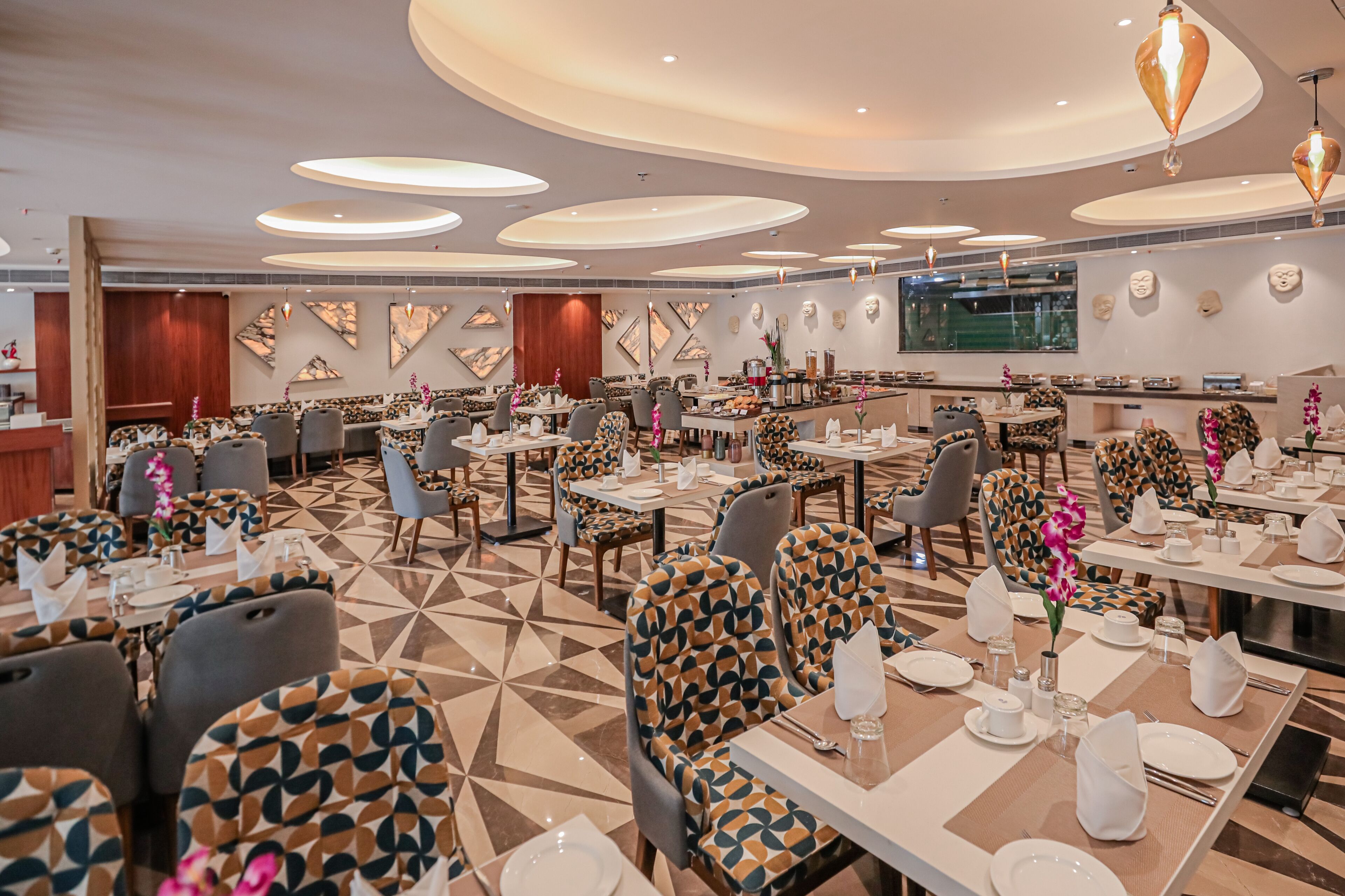 Uma sala de jantar moderna, com assentos estampados, mesas preparadas para refeições e obras de arte decorativas nas paredes.