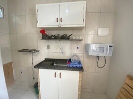 Uma cozinha compacta com armários brancos, micro-ondas embutido e pia.