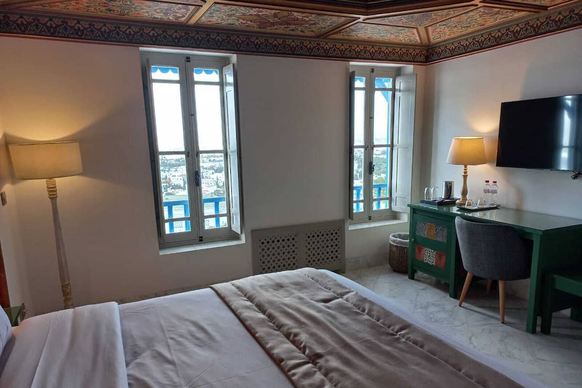 Quarto de hotel com cama, escrivaninha, televisão e janela com vista.