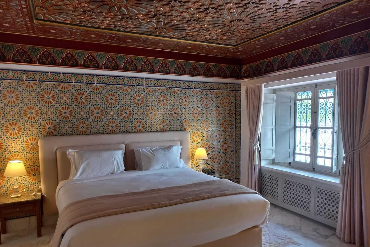 Um quarto com uma cama grande, paredes estampadas, uma janela com cortinas e um teto decorativo.