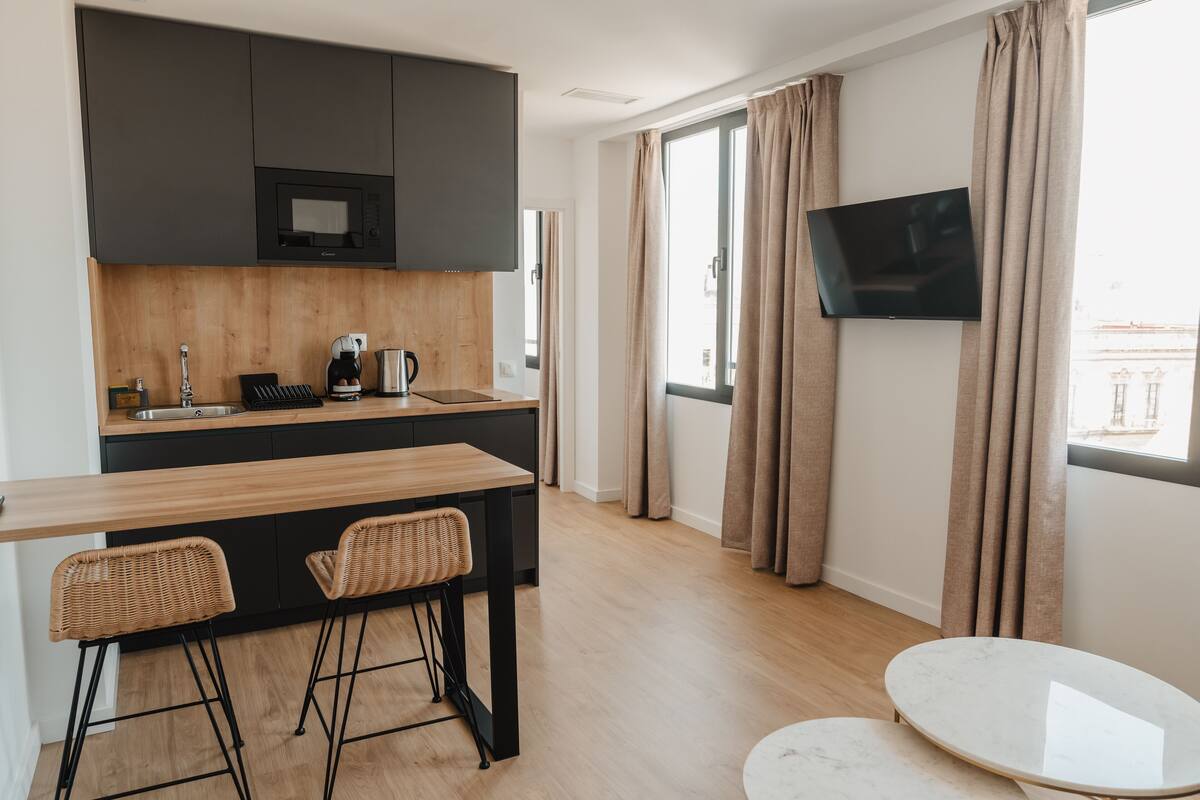 Uma cozinha moderna com bancada de madeira, dois banquetas altas, uma pequena mesa redonda e uma TV fixada na parede.