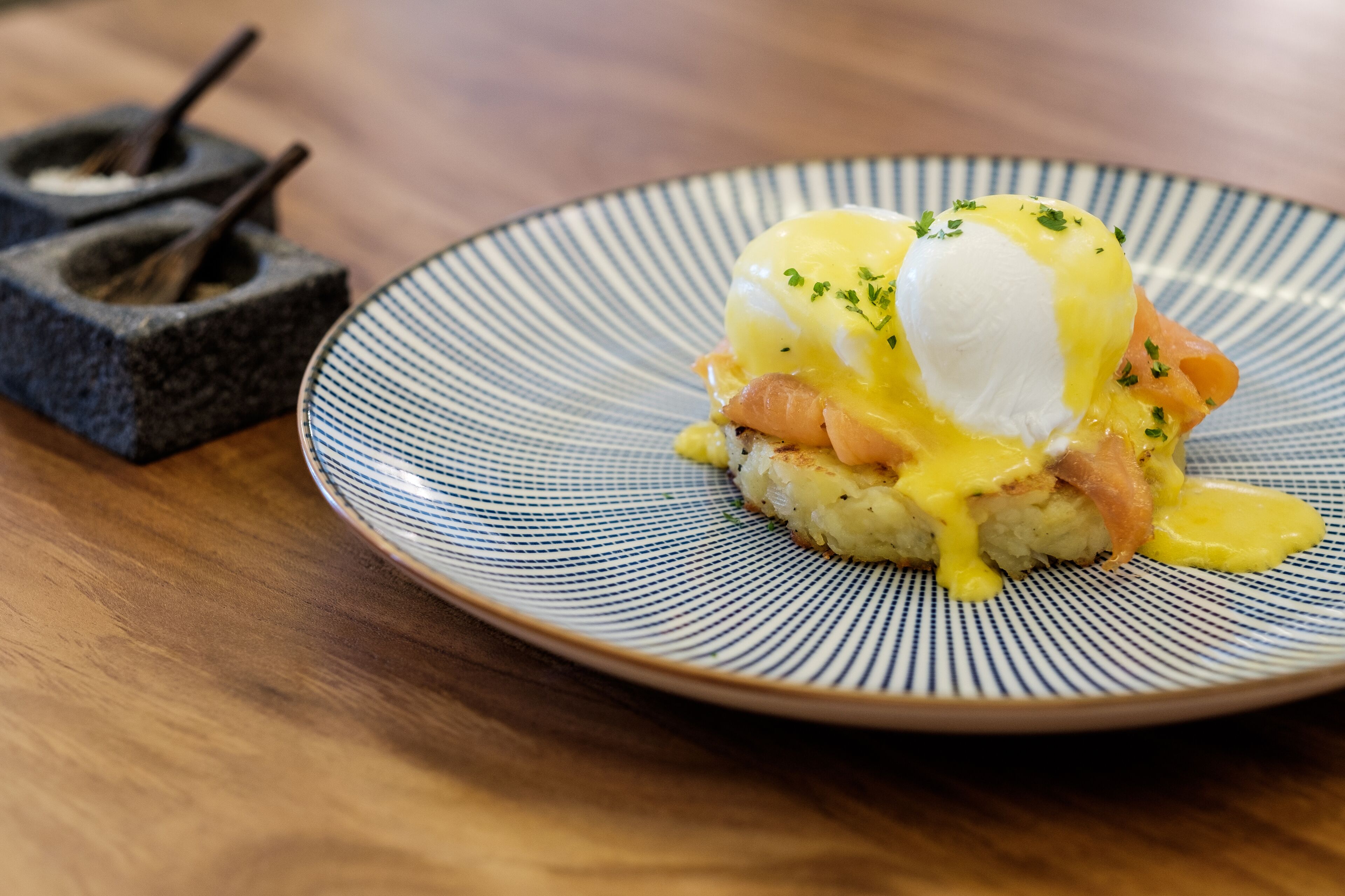 Um prato de ovos Benedict com molho holandês e ovos pochê em um prato listrado.