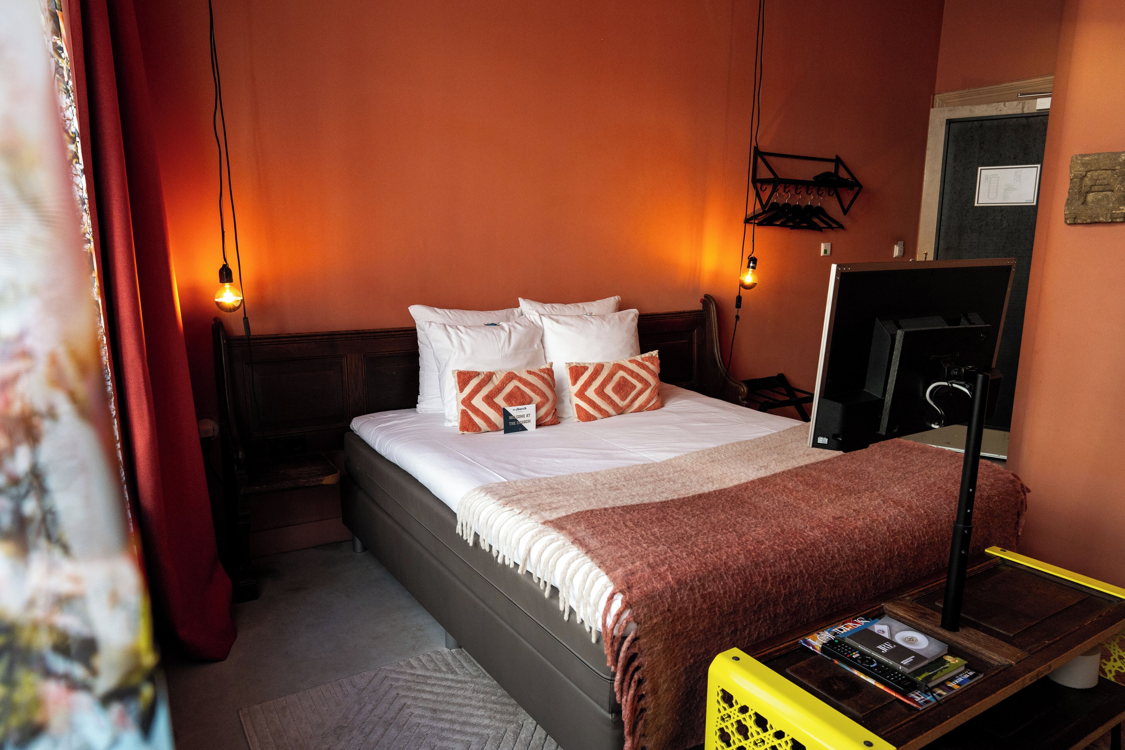 Quarto de hotel com cama, televisão e uma pequena mesa com controle remoto.