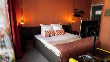 Quarto de hotel com cama, televisão e uma pequena mesa com controle remoto.