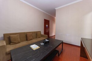 Quarto com um sofá castanho, uma mesa de centro em madeira escura e uma porta de madeira ao fundo.
