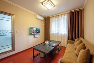 Um quarto com piso de madeira, um sofá, uma mesa com um laptop, um quadro na parede e uma janela com cortinas.