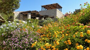 Um edifício de pedra com pérgola de madeira, rodeado por flores coloridas.