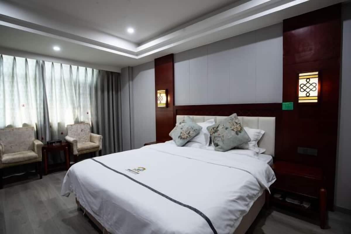 Quarto de hotel com uma cama grande, duas poltronas, uma mesinha e uma mesa de cabeceira.