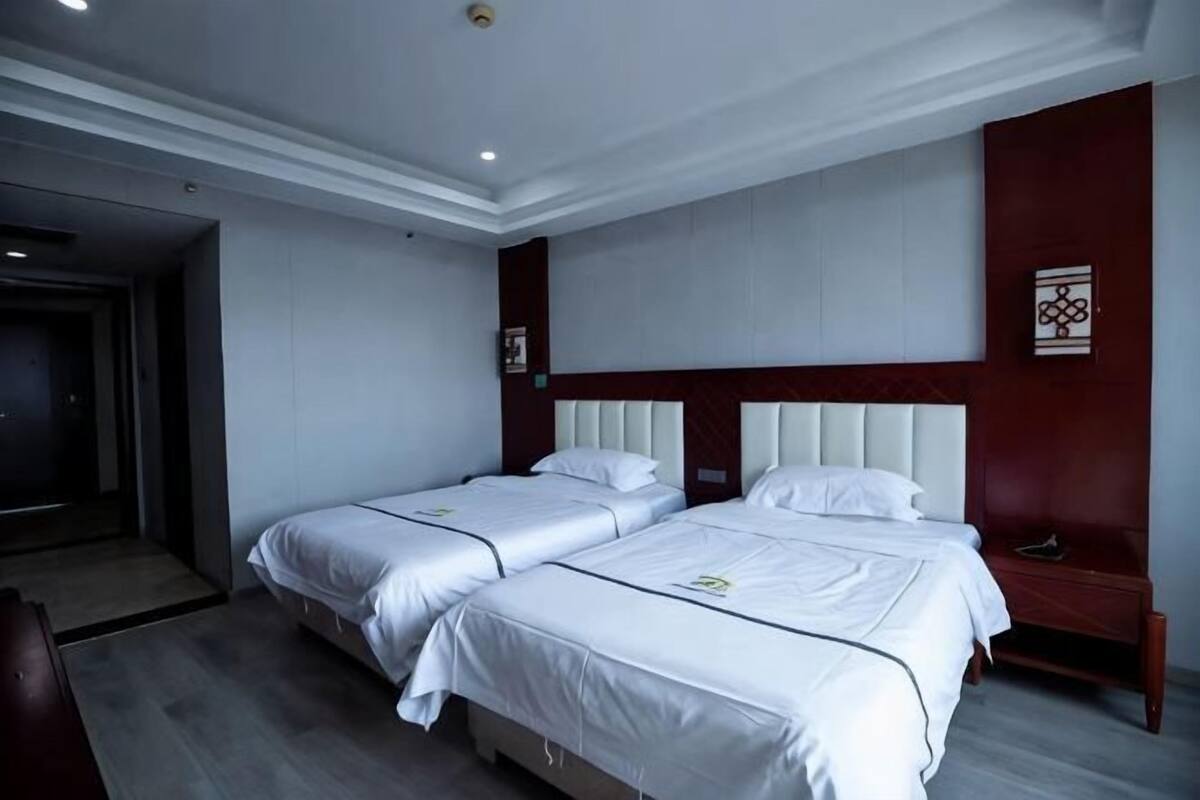 Quarto de hotel com duas camas, cabeceira de madeira, mesa de cabeceira e porta que dá para outro cômodo.