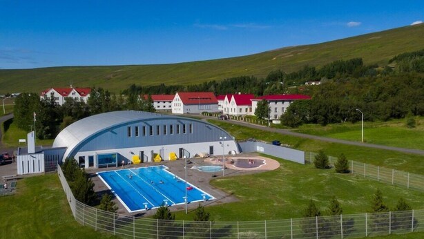 Um edifício grande com piscina, rodeado por uma área cercada e uma paisagem montanhosa.