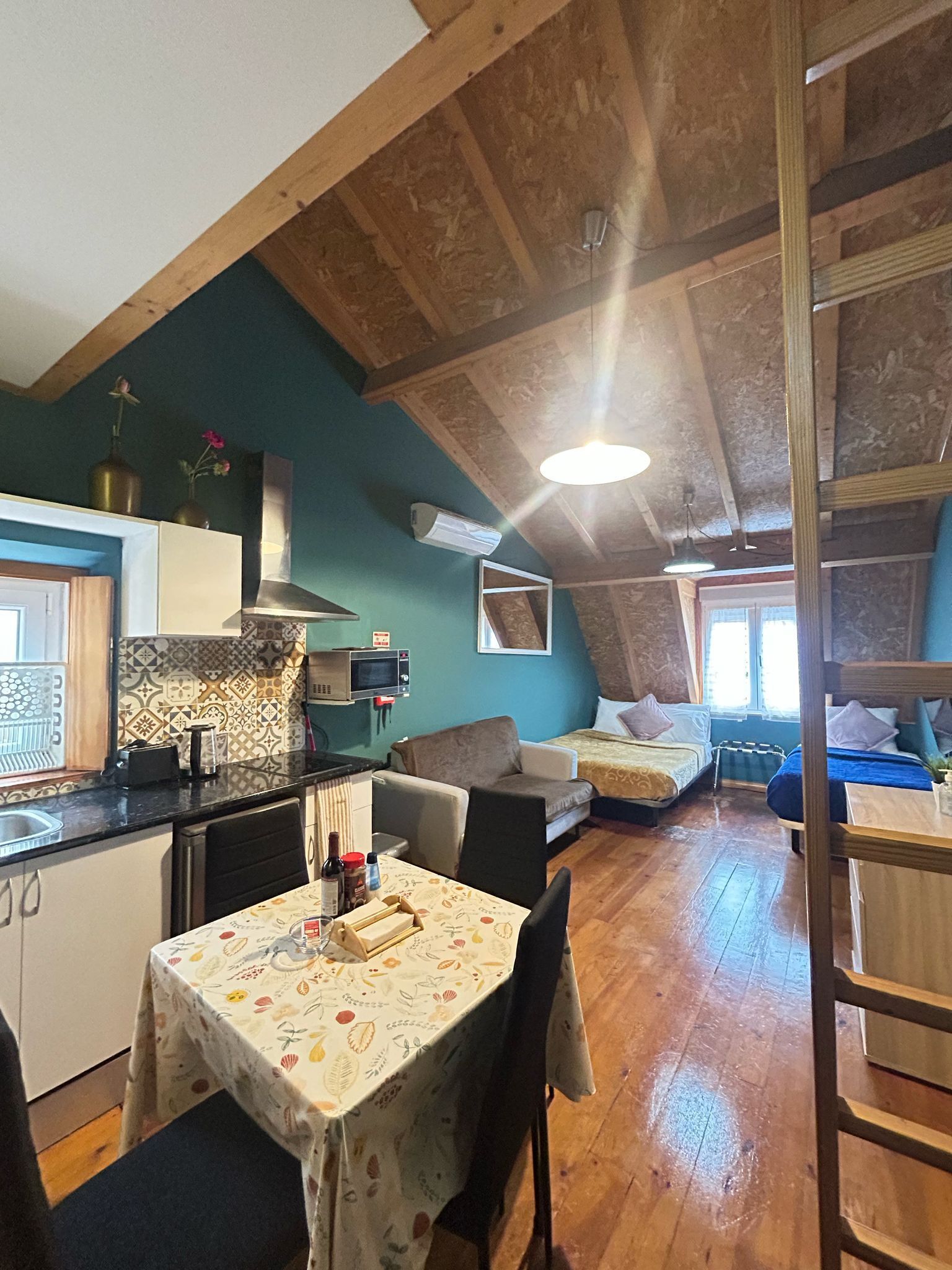 Um quarto acolhedor e rústico, com cozinha, mesa de jantar e cadeiras, e uma cama em mezanino.