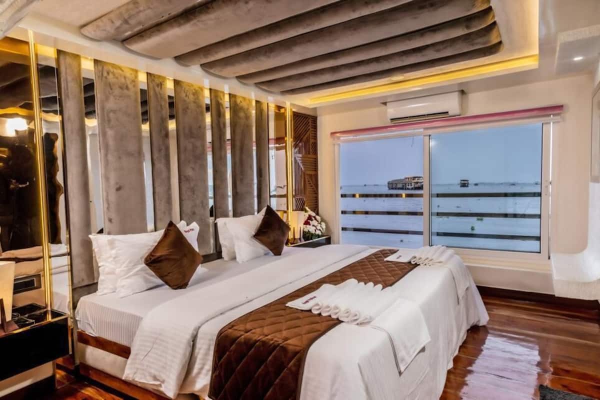 Quarto de hotel moderno com uma cama grande, vista para o mar e piso de madeira.