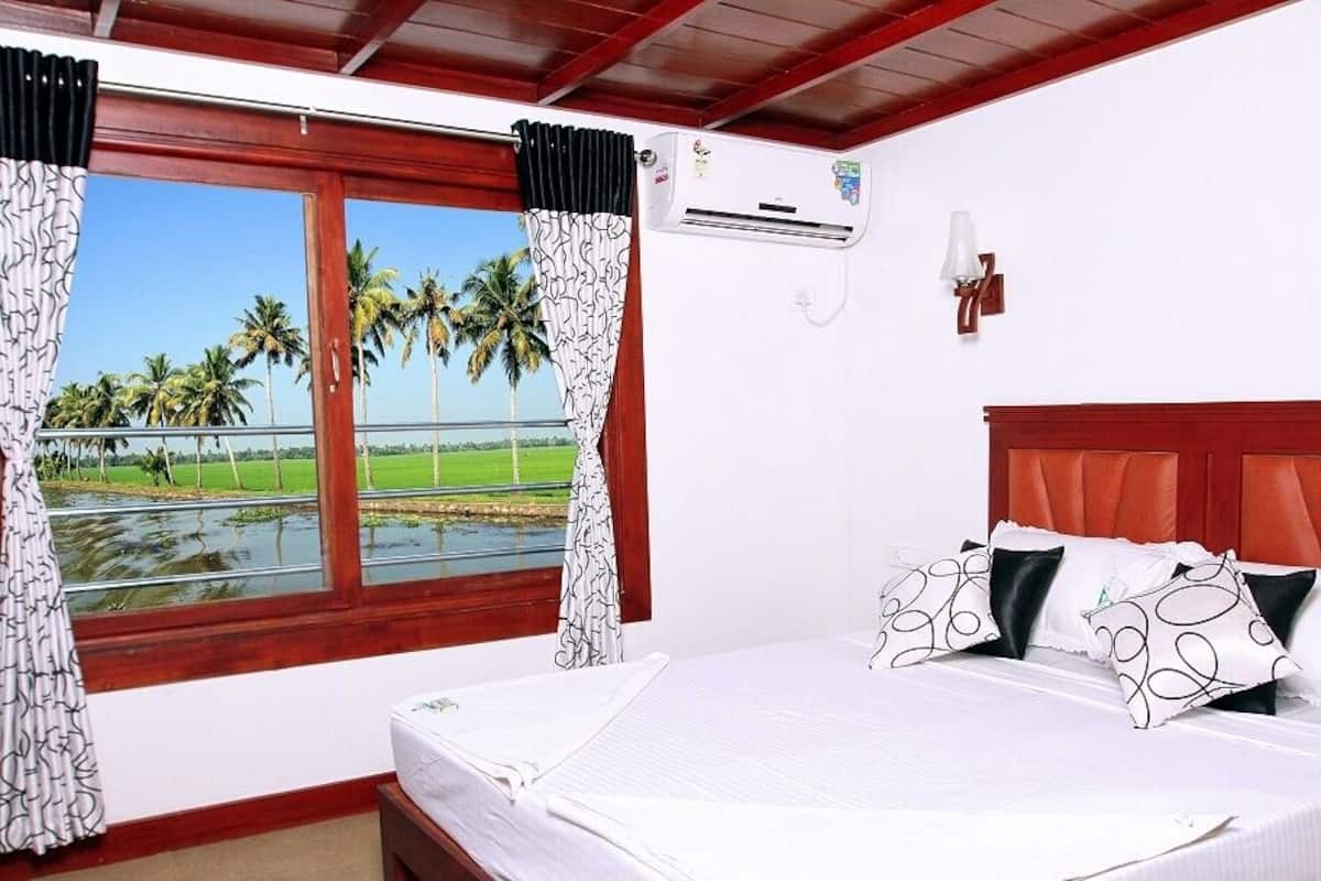 Quarto com uma cama grande, vista para palmeiras e água lá fora, e um ar condicionado na parede.