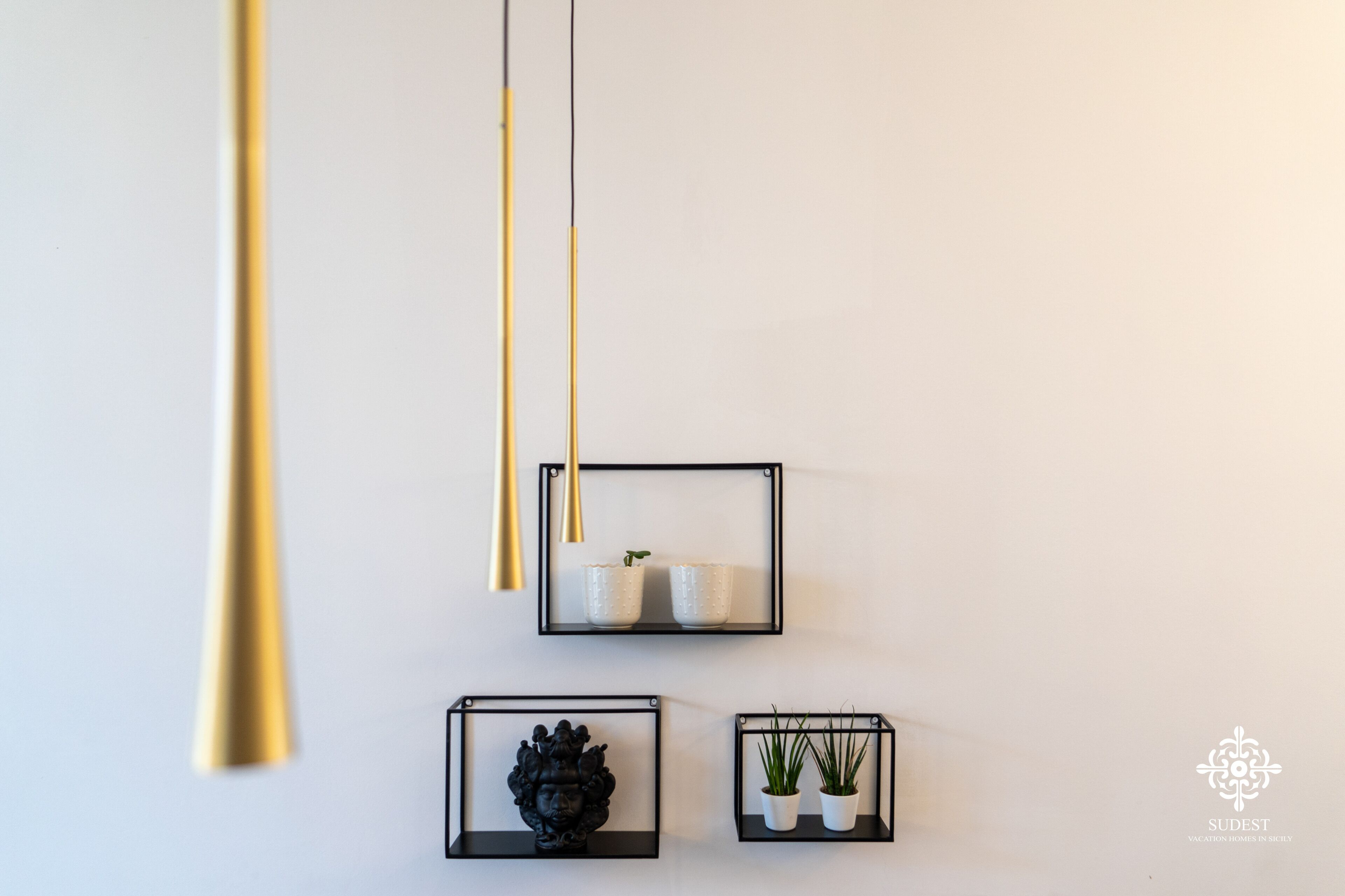 Três prateleiras de parede com moldura preta, adornadas com objetos decorativos e plantas em vasos.