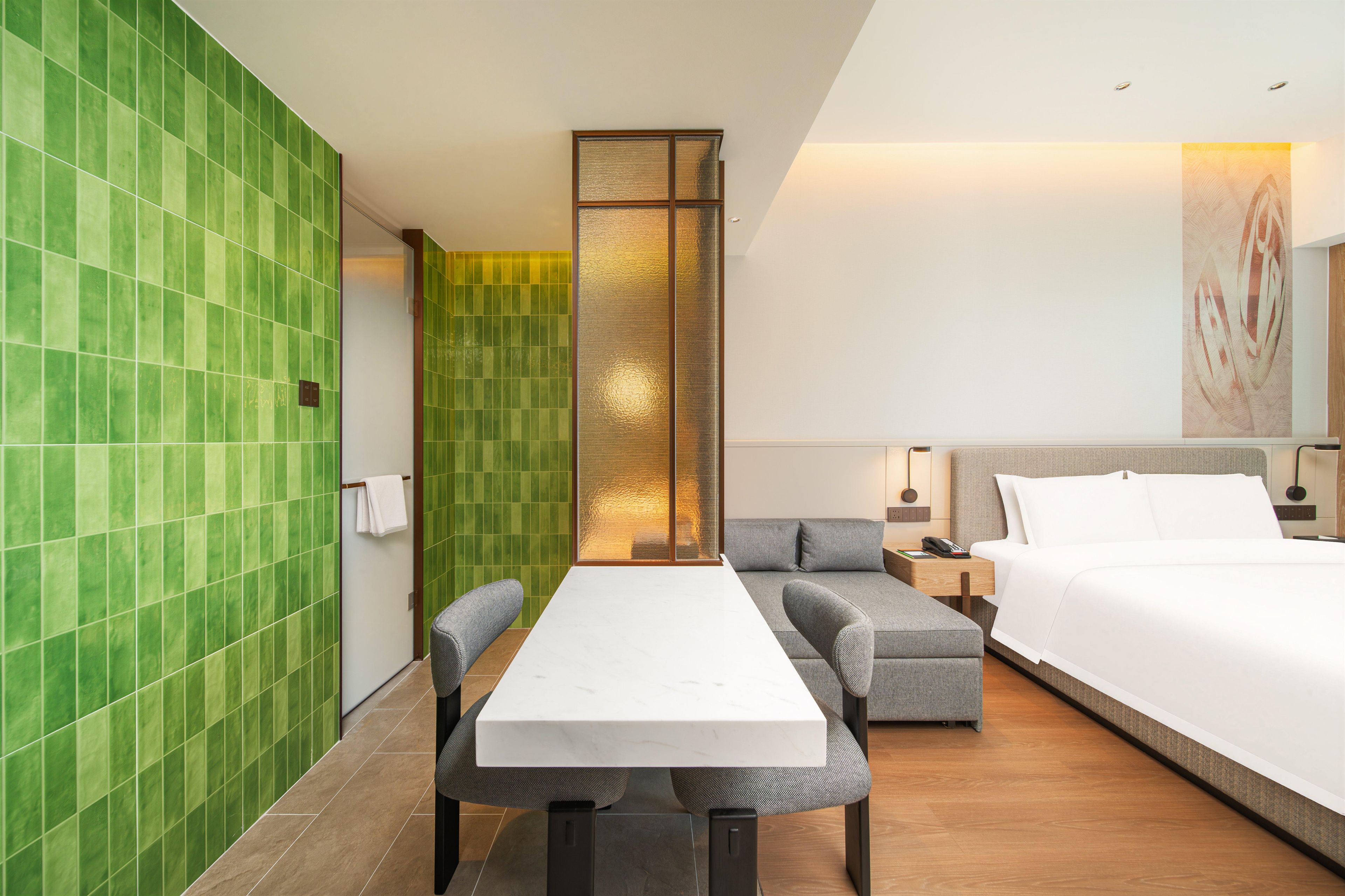 Quarto de hotel com cama, sofá, mesa de jantar e parede com azulejos verdes.