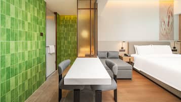 Quarto de hotel com cama, sofá, mesa de jantar e parede com azulejos verdes.