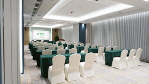 Uma sala de conferência com mesas e cadeiras dispostas em fileiras, uma tela de projetor e uma área para apresentações.