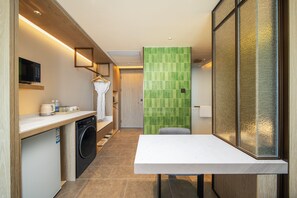 Quarto de hotel moderno com cozinha, máquina de lavar, mesa e divisória verde.