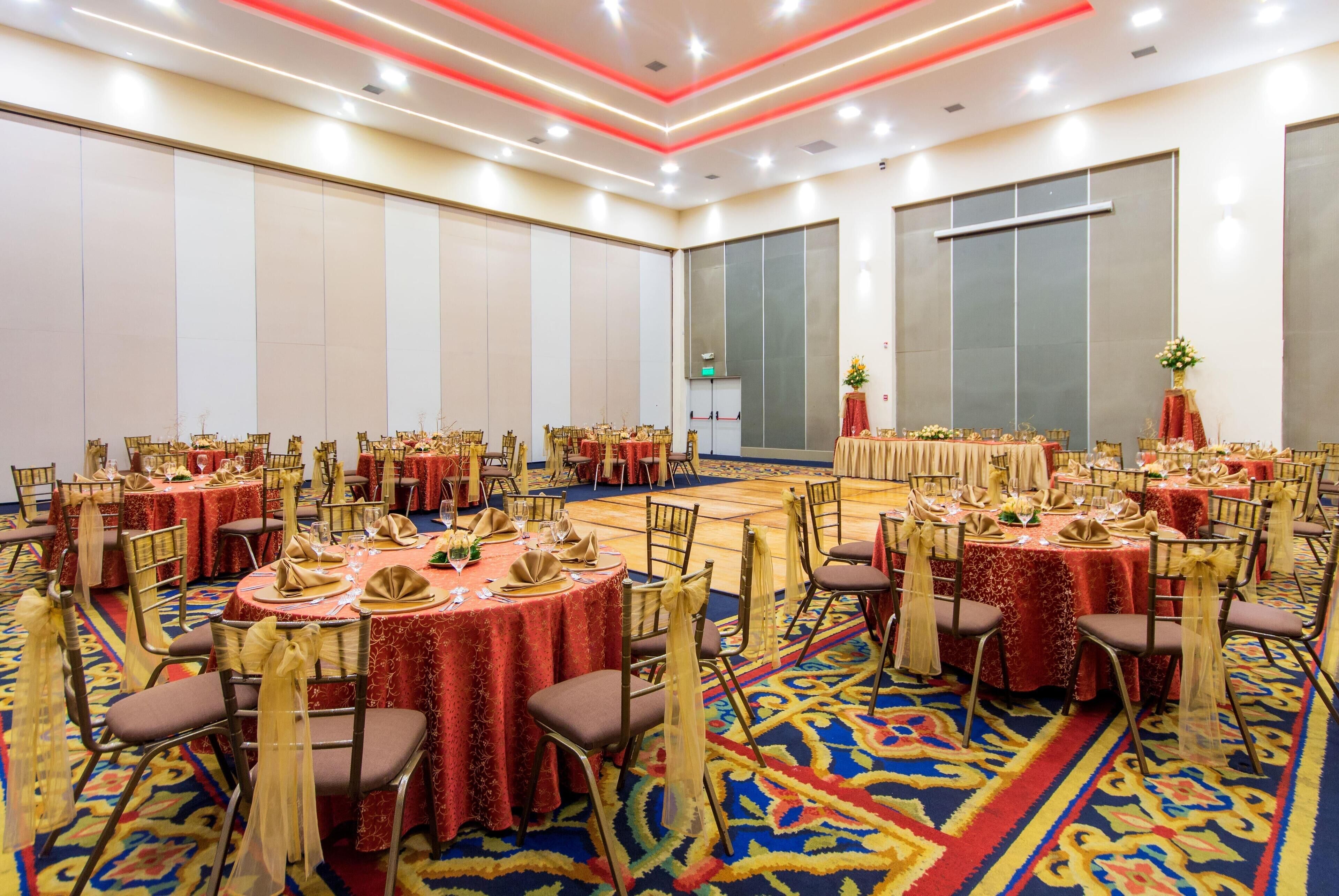 Uma sala de banquetes com mesas redondas, cadeiras e piso coberto por carpete.