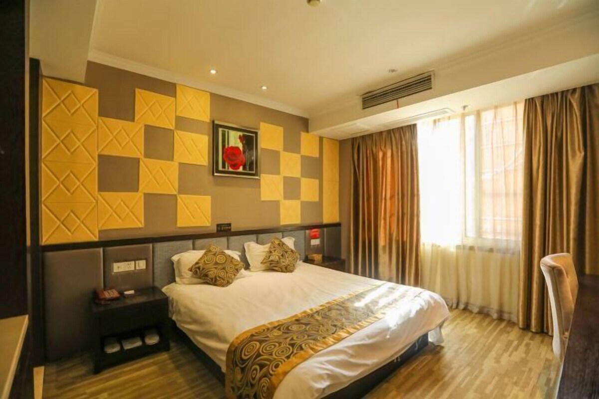 Quarto de hotel com uma cama grande, uma mesa de cabeceira, uma cadeira e uma janela com cortinas.